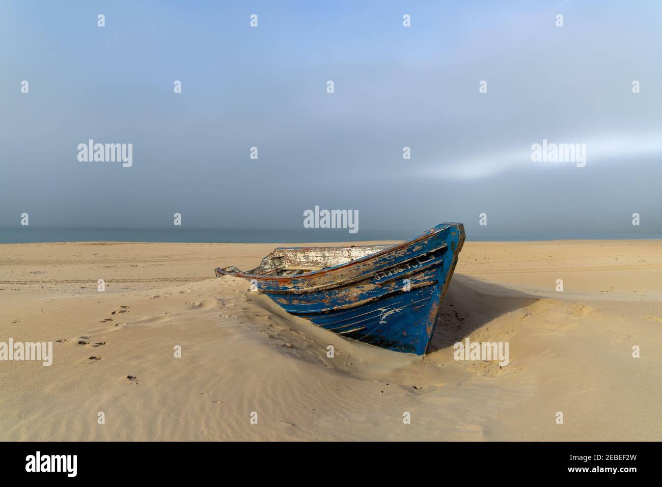 An colorful old wooden rowboat buried in the sand on a beach after ...