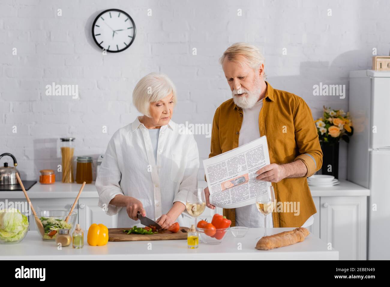 Senior couple reading newspaper while cooking salad Stock Photo - Alamy