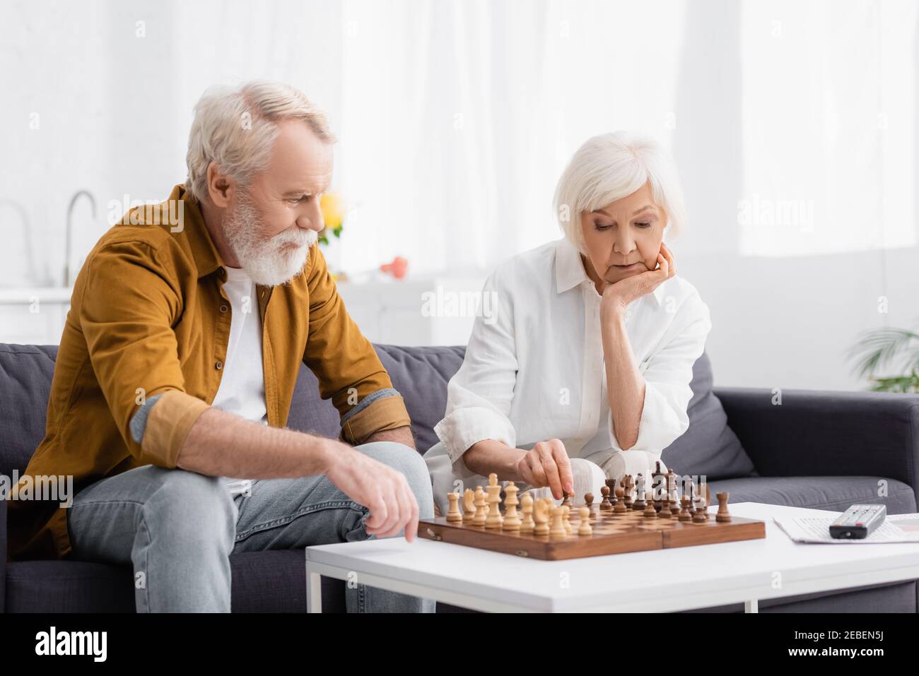 Pensive elderly couple playing chess near remote controller on blurred ...