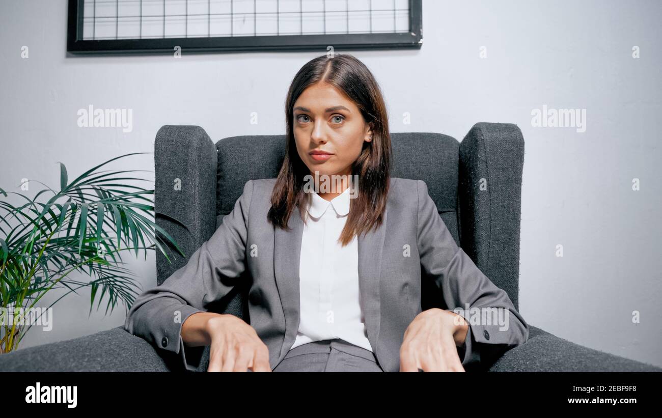 Brunette manager sitting on armchair near plant Stock Photo - Alamy