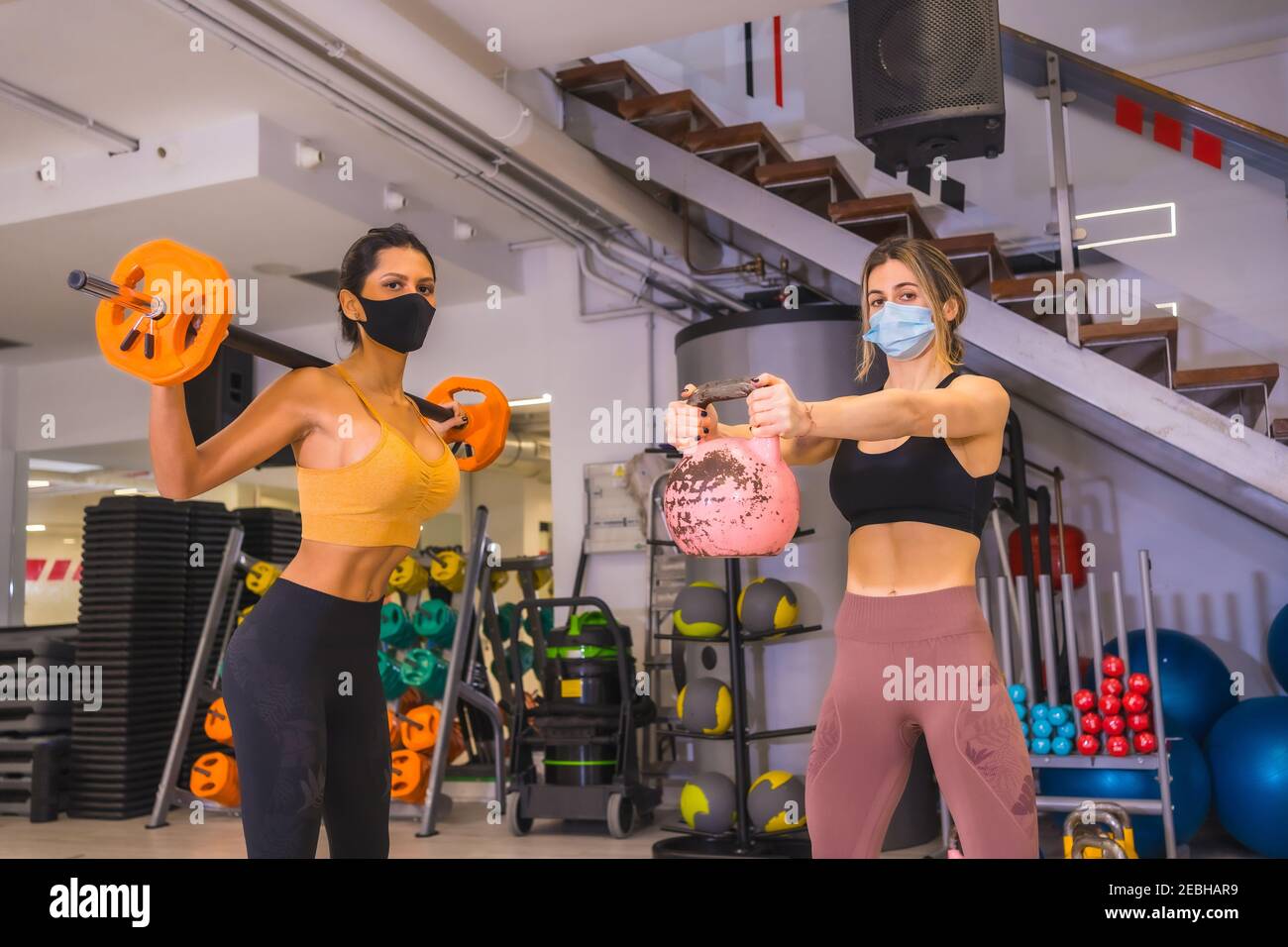 Athletic females training muscles with weights with face masks ...