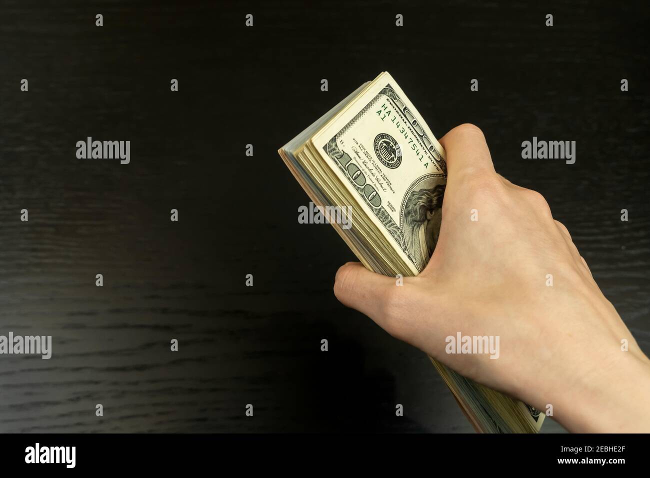 Woman's hand with a wad of hundred-dollar bills on a dark background ...