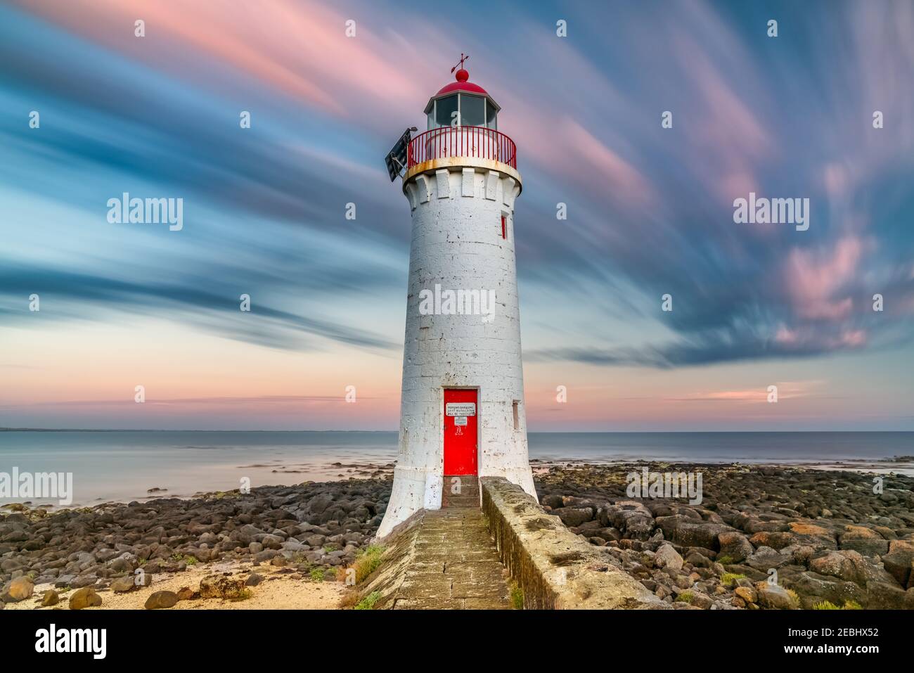 Classic Red and White lighthouse long exposure sunset with rock beach ...