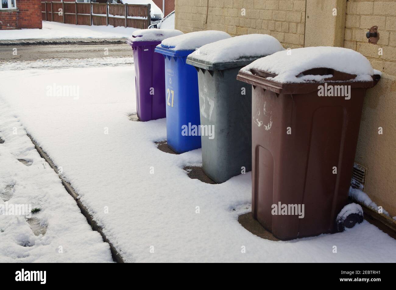 Four different snow-covered waste recycling bins alongside a house wall ...