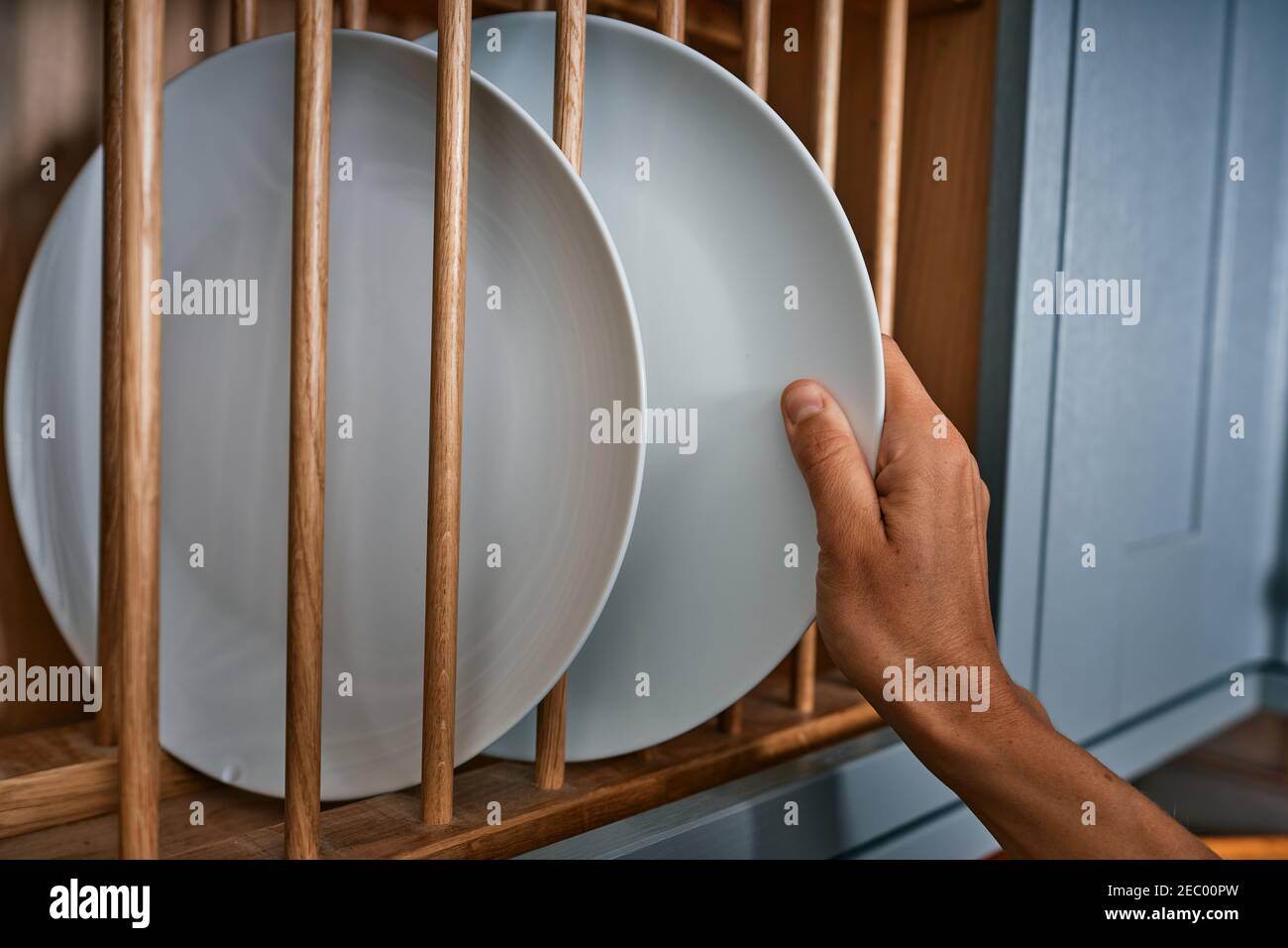 The hand of a young woman is grabbing a plate from a rack at home in ...