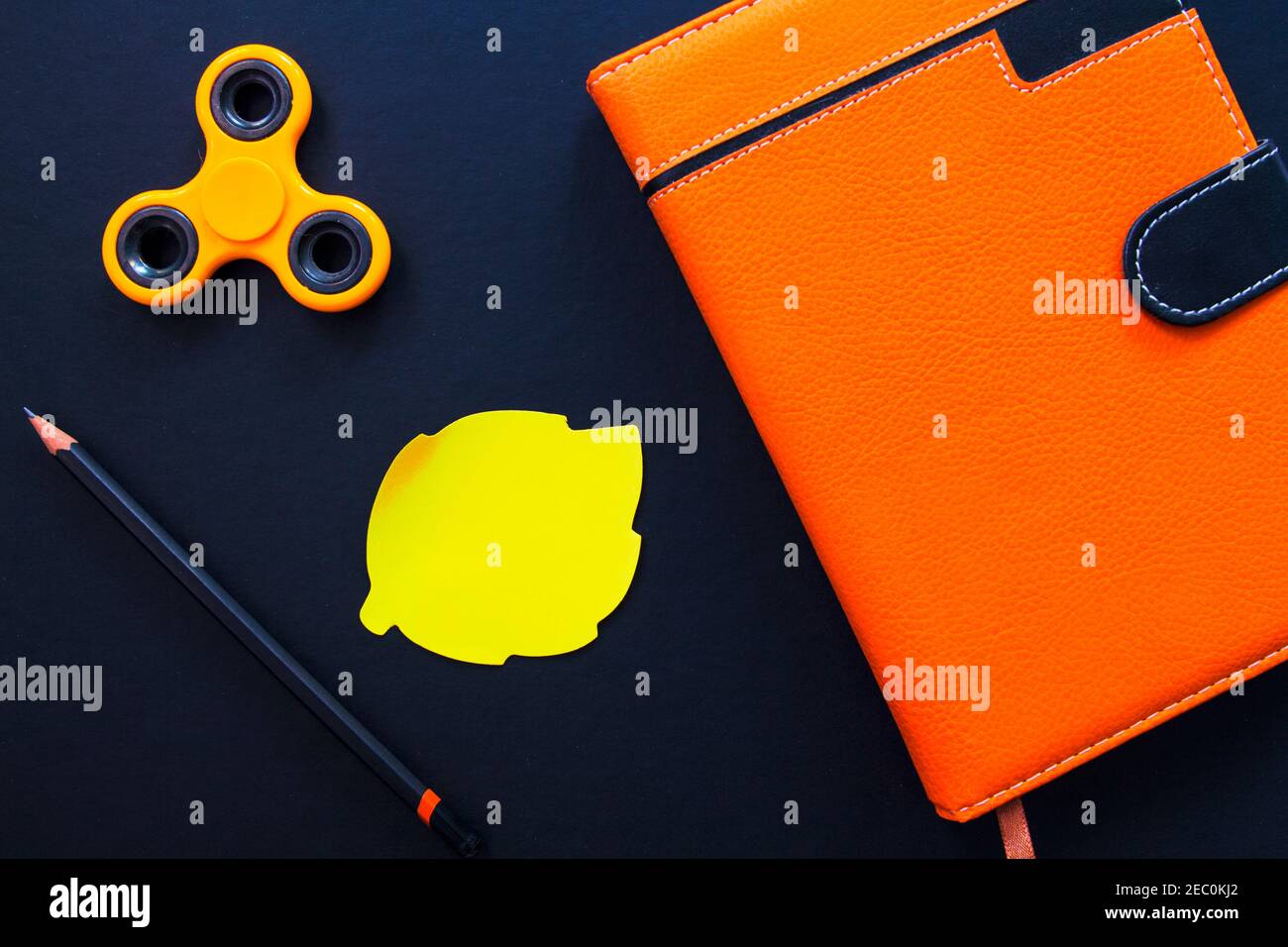 Orange notebook and spinner flat lay photo on black background. Spinner ...