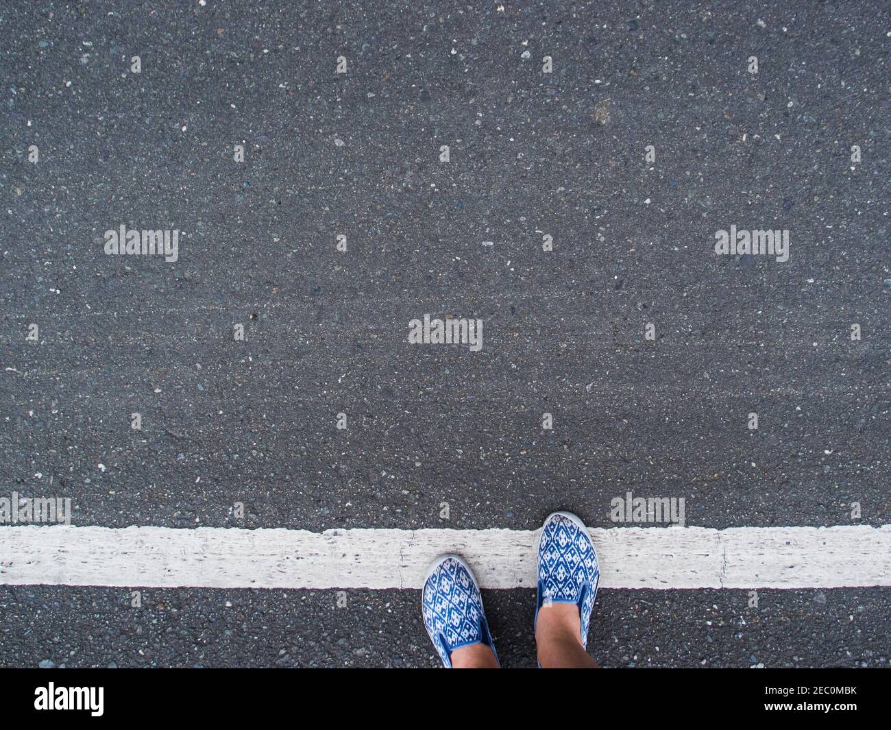 Grey asphalt with white line mark and woman feet in shoes. Girl feet in ...