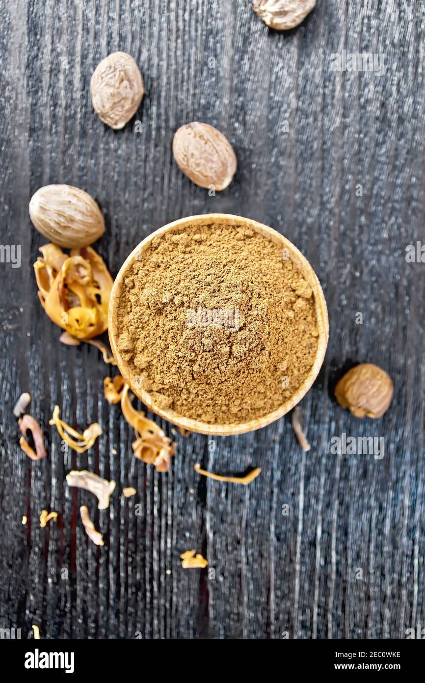 Ground nutmeg in a bowl, dried nutmeg arillus and whole nuts on a dark ...