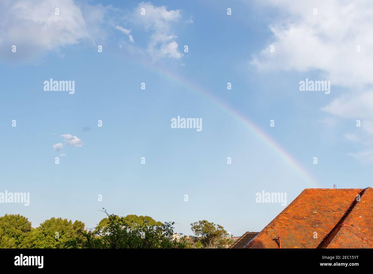 Rainbow over a house with a red tile roof above some large trees Stock ...