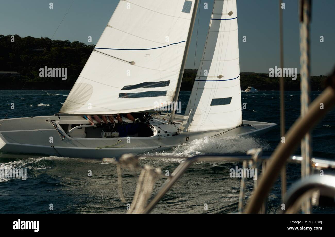Sleek yacht racing in covered waters. Full boat in view with land in ...