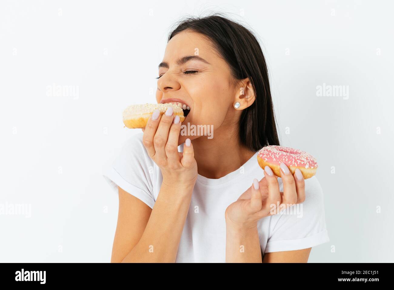 Portrait of beautiful young brunette woman biting eating donuts ...