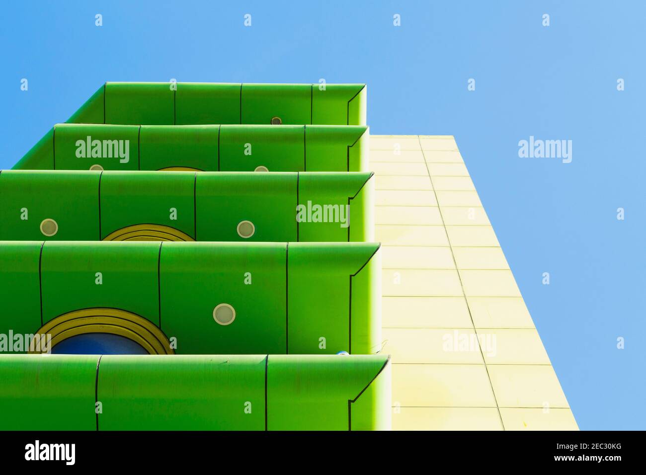 Modern green and yellow building with balconies on blue sky background ...
