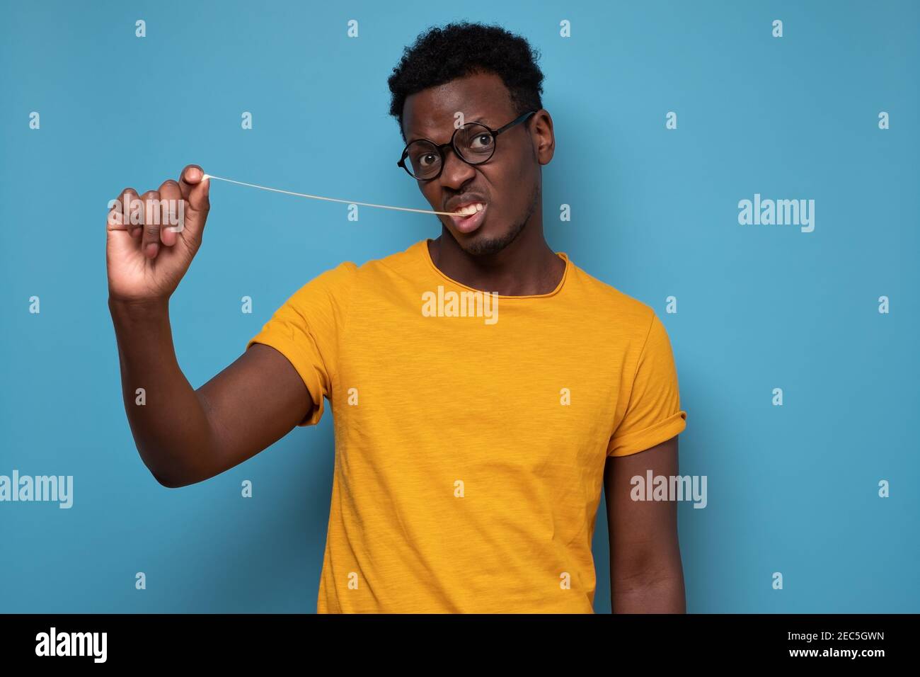 Young african man pulling a chewing gum. Studio shot on blue wall Stock ...