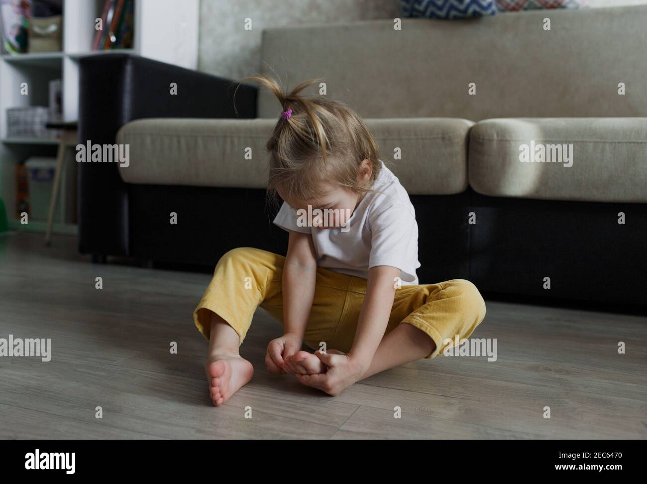 a little girl in a white T-shirt and yellow pants sits on the floor of ...