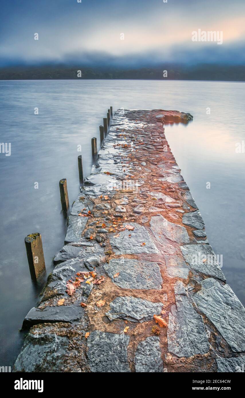 Stone built jetty stretching out into the still waters of Coniston ...