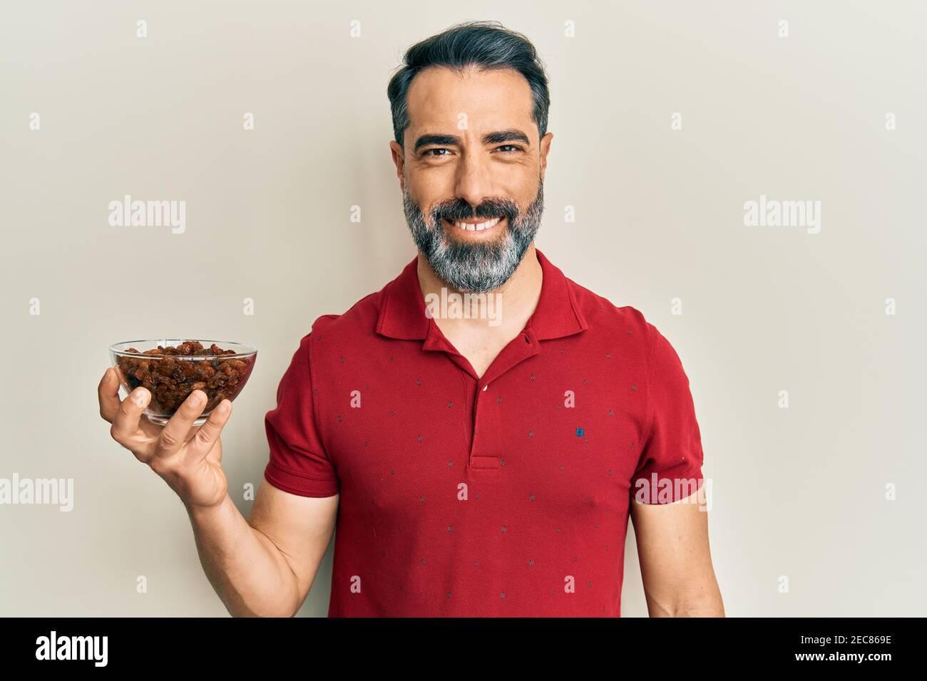 Middle age man with beard and grey hair holding raisins bowl looking ...