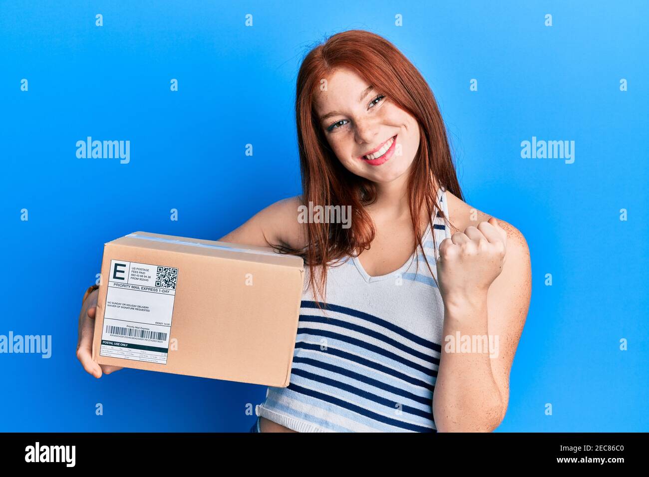 Young red head girl holding delivery package screaming proud ...