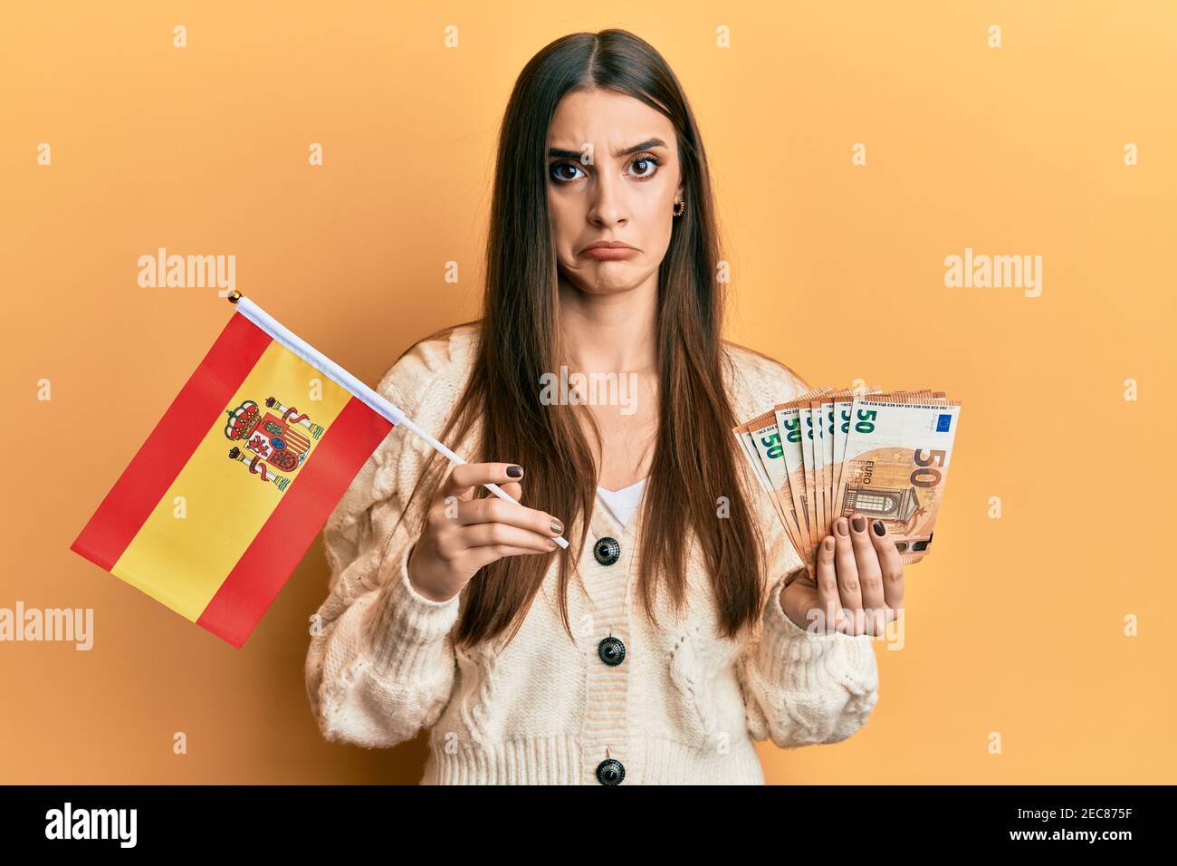 Beautiful brunette young woman holding spain flag and euros banknotes ...