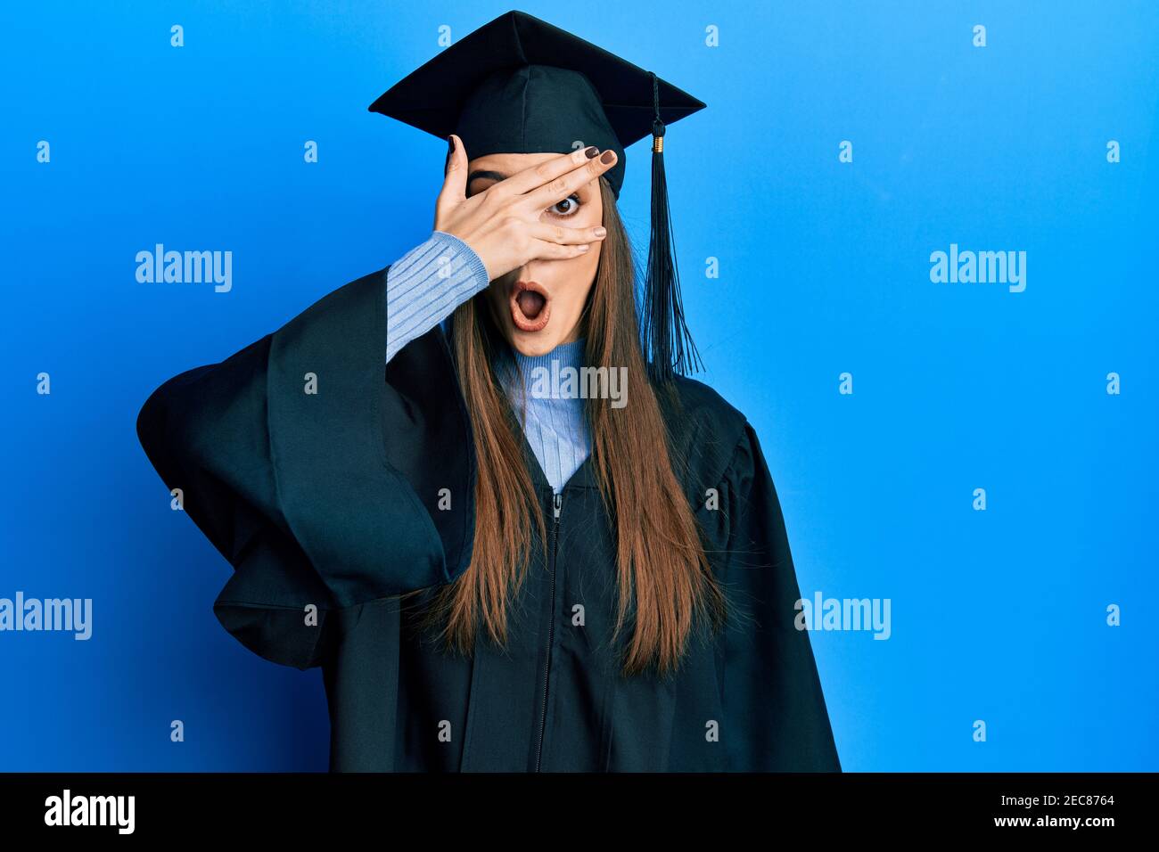 Beautiful brunette young woman wearing graduation cap and ceremony robe ...