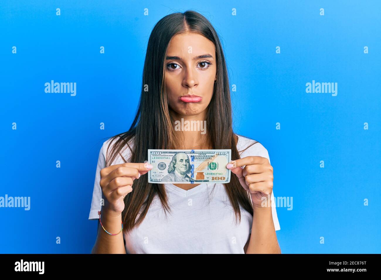 Young hispanic woman holding 100 dollar banknote depressed and worry ...