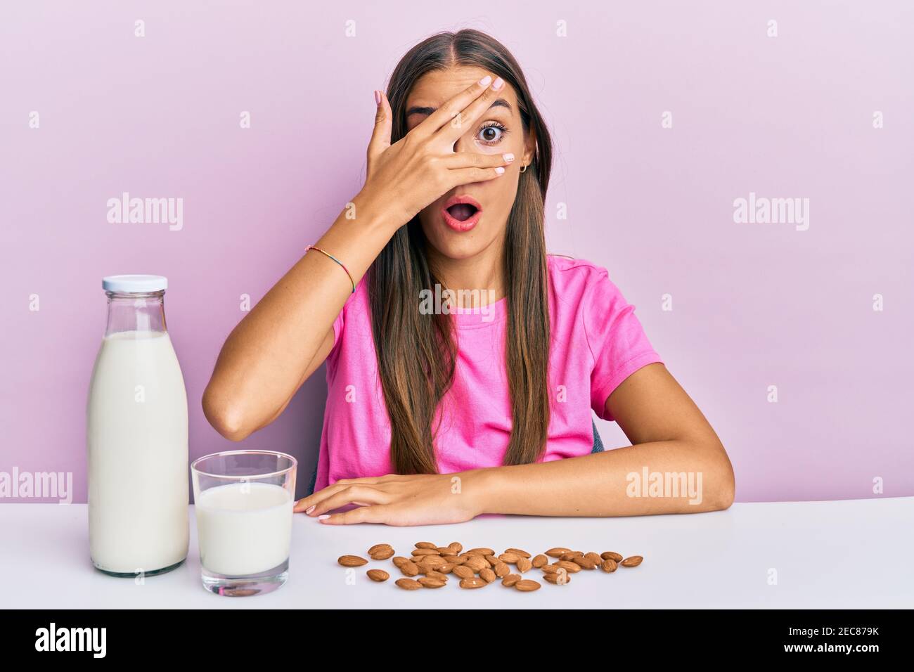 Young hispanic woman drinking healthy almond milk sitting on the table ...