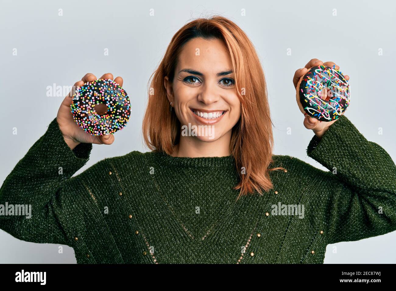 Hispanic young woman holding tasty colorful doughnuts smiling with a ...