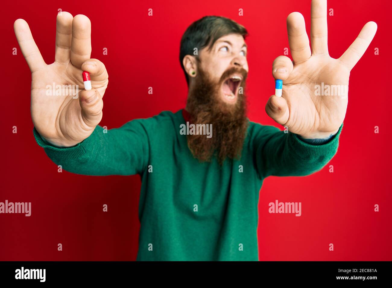Redhead man with long beard holding two different pills angry and mad ...