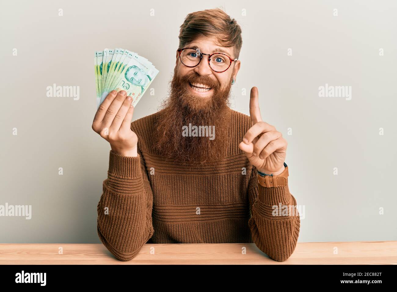 Young irish redhead man holding 5 singapore dollars banknotes sitting ...
