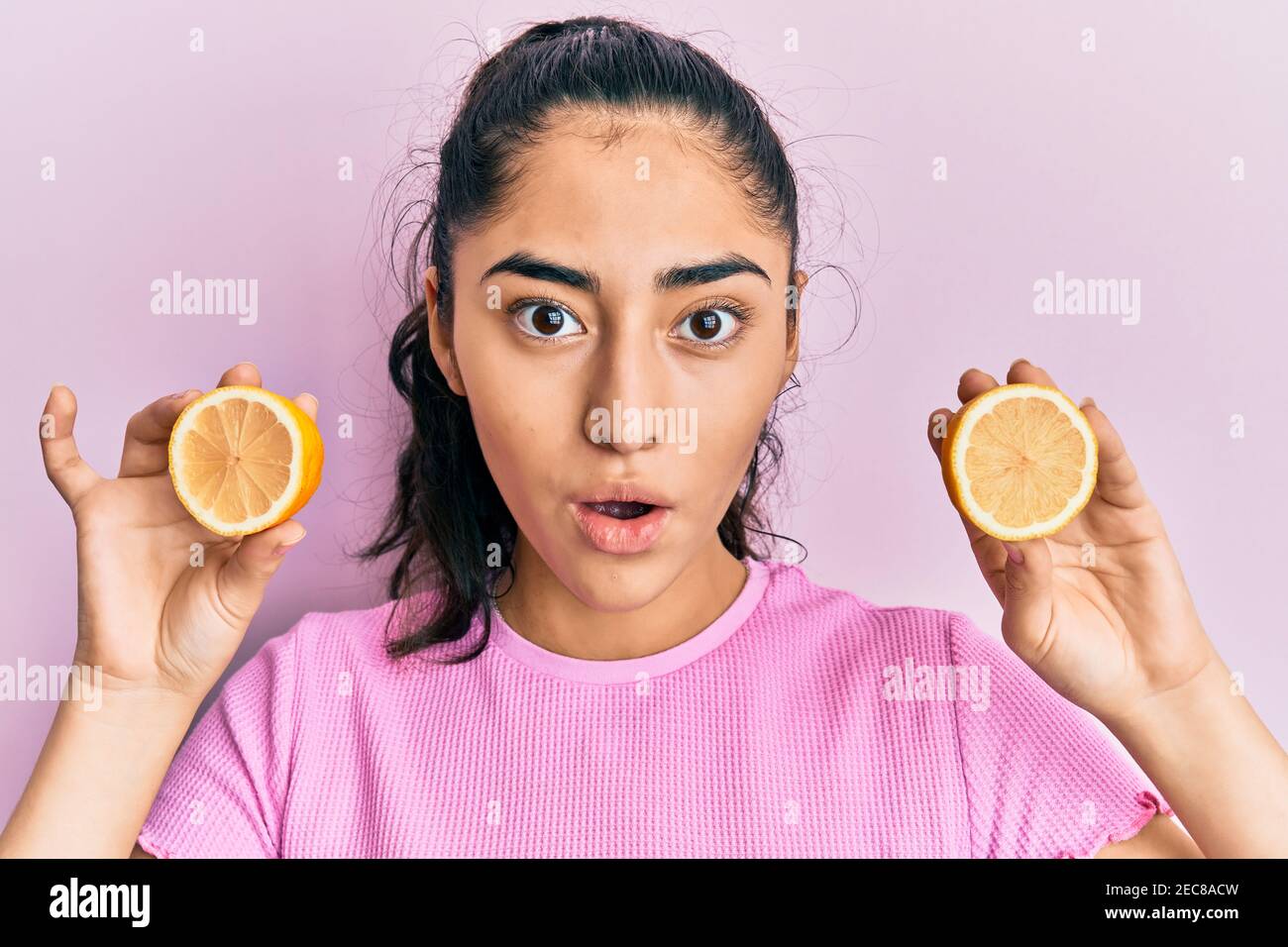 Hispanic teenager girl with dental braces holding lemon afraid and ...