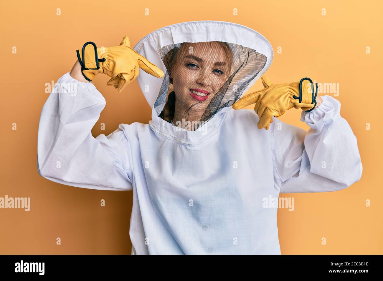 Beautiful blonde caucasian woman wearing protective beekeeper uniform ...