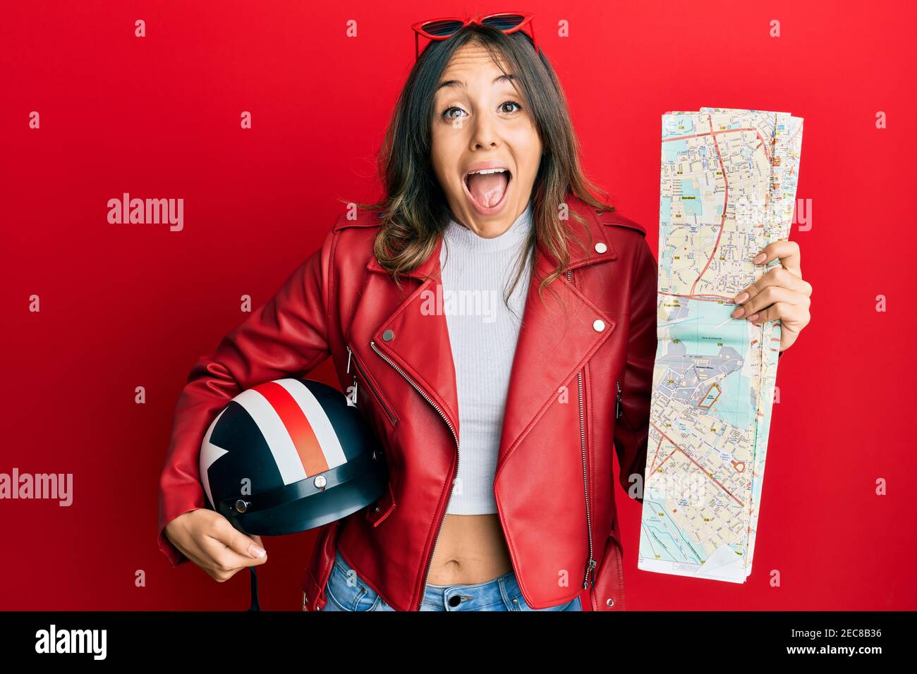 Young brunette woman holding motorcycle helmet and city map celebrating ...