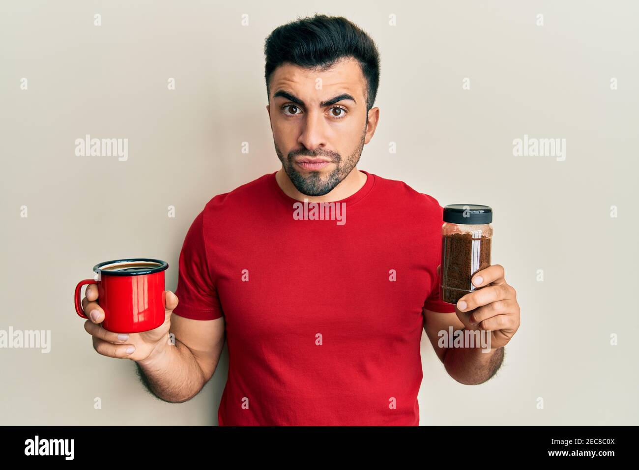 Young hispanic man holding cup of soluble coffee skeptic and nervous ...