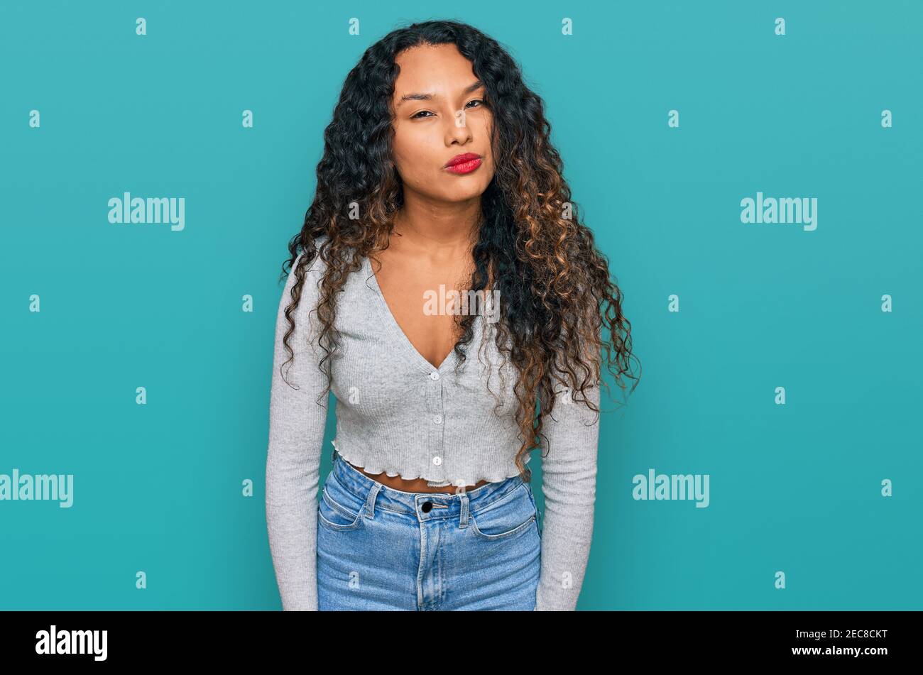 Young hispanic woman with curly hair wearing casual clothes skeptic and ...