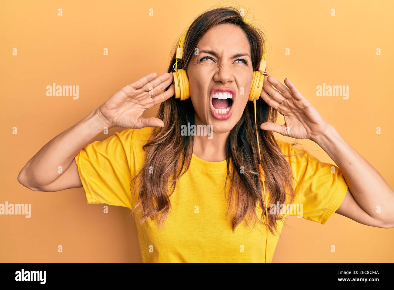 Young latin woman listening to music using headphones angry and mad ...