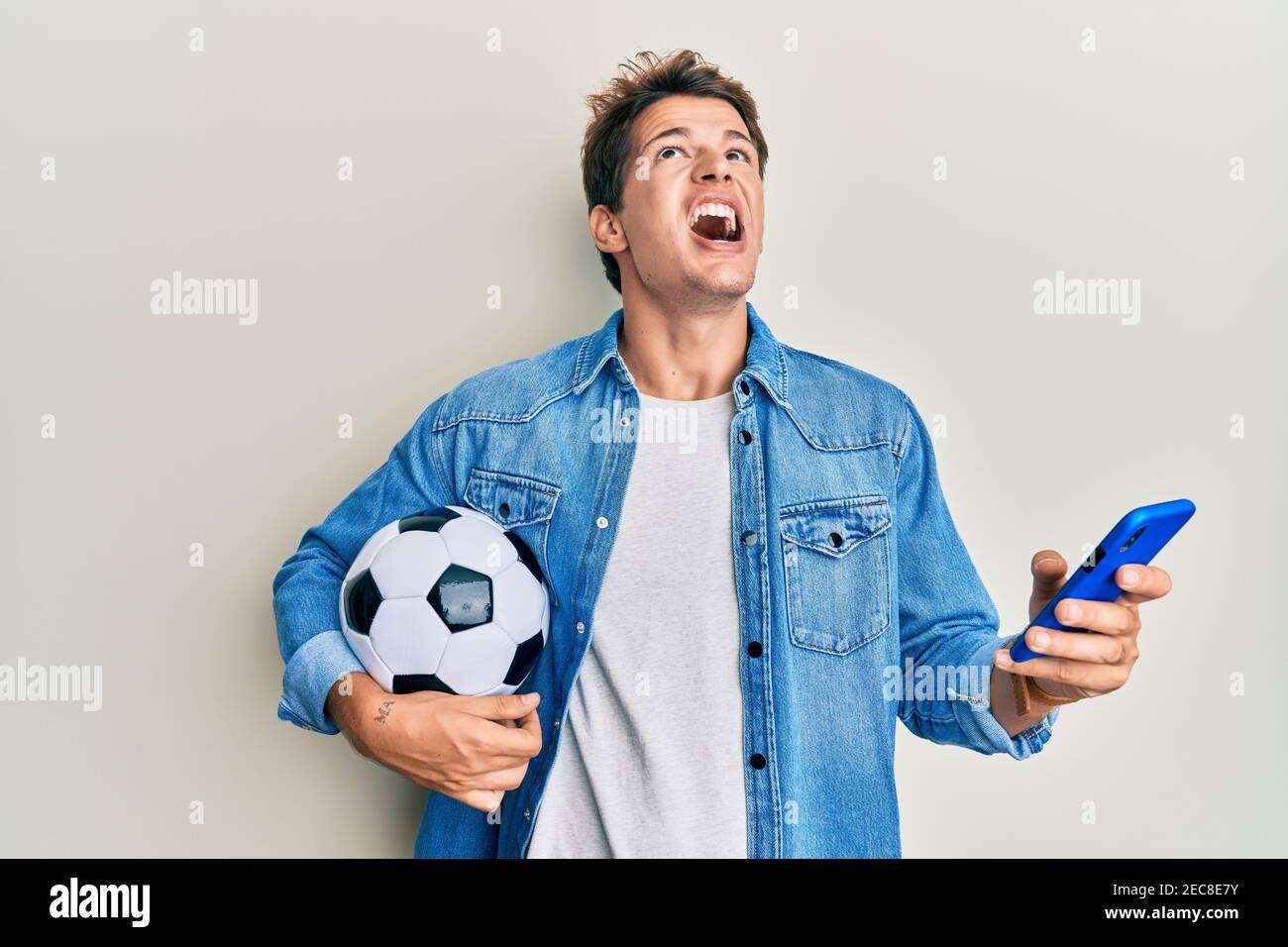 Handsome caucasian man holding football ball looking at smartphone ...