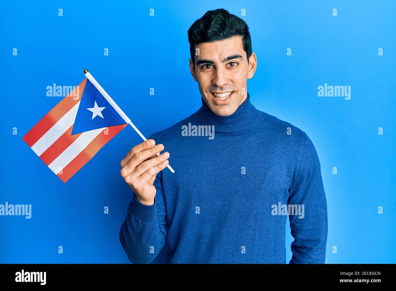 Handsome hispanic man holding puerto rico flag looking positive and ...