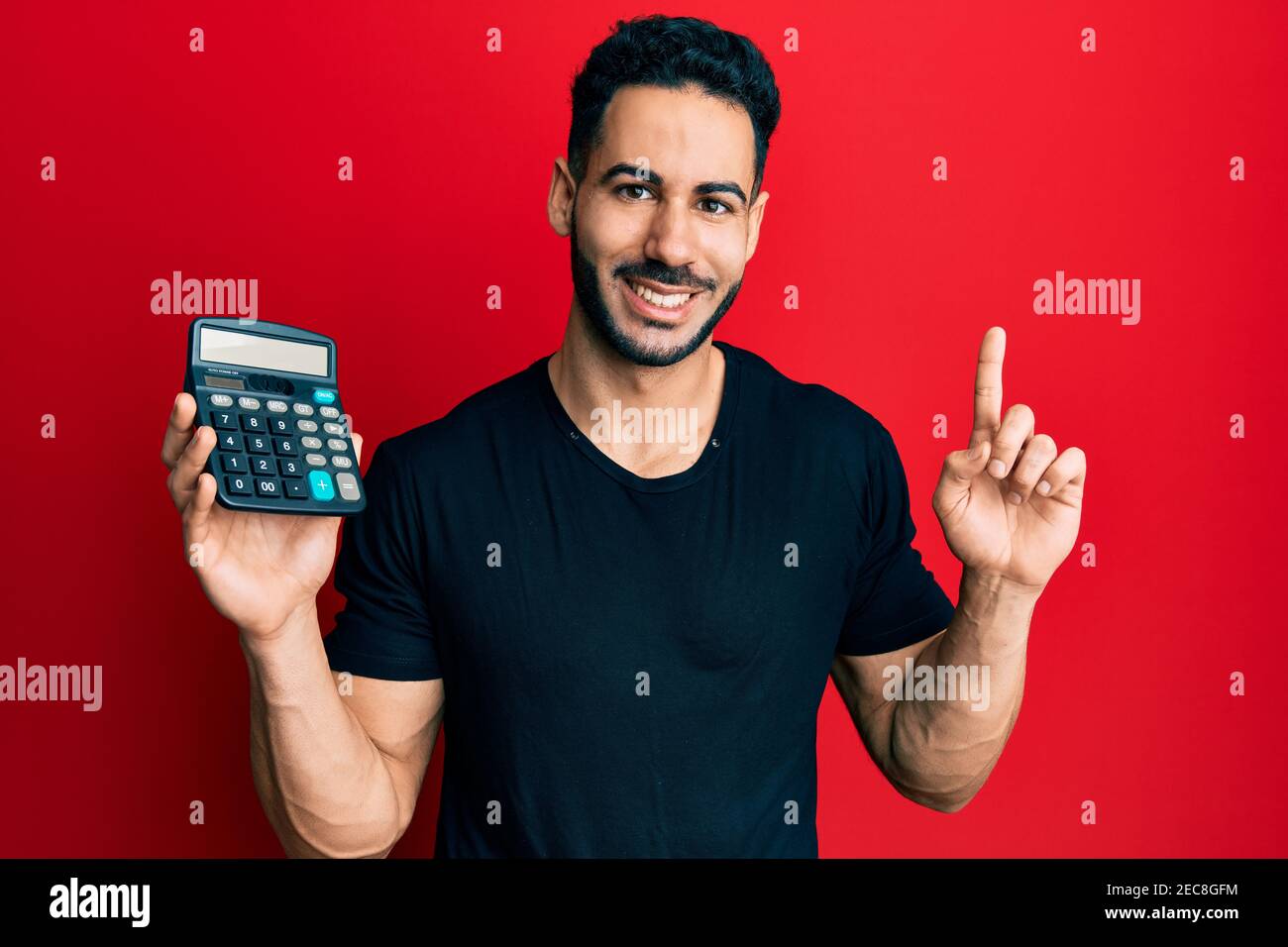 Young hispanic man showing calculator device smiling with an idea or ...