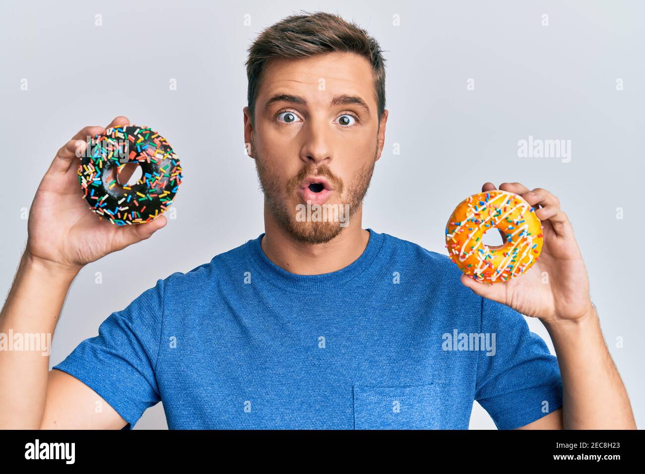 Handsome caucasian man holding tasty colorful doughnuts afraid and ...