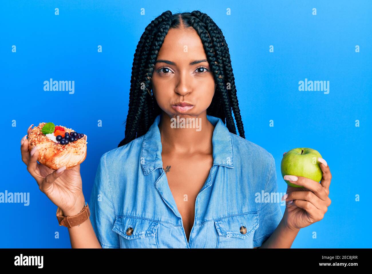 Beautiful hispanic woman holding pastry and healthy green apple puffing ...