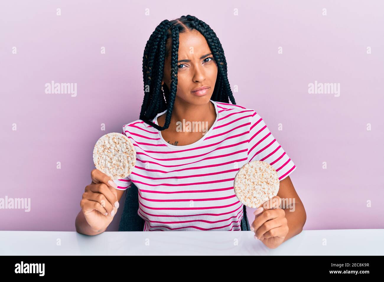 Beautiful hispanic woman eating healthy rice crackers in shock face ...