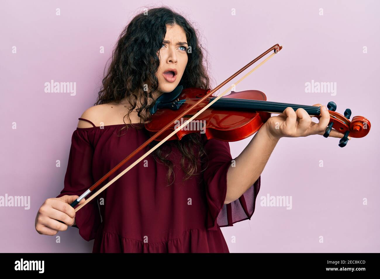Young brunette musician woman with curly hair playing violin angry and ...