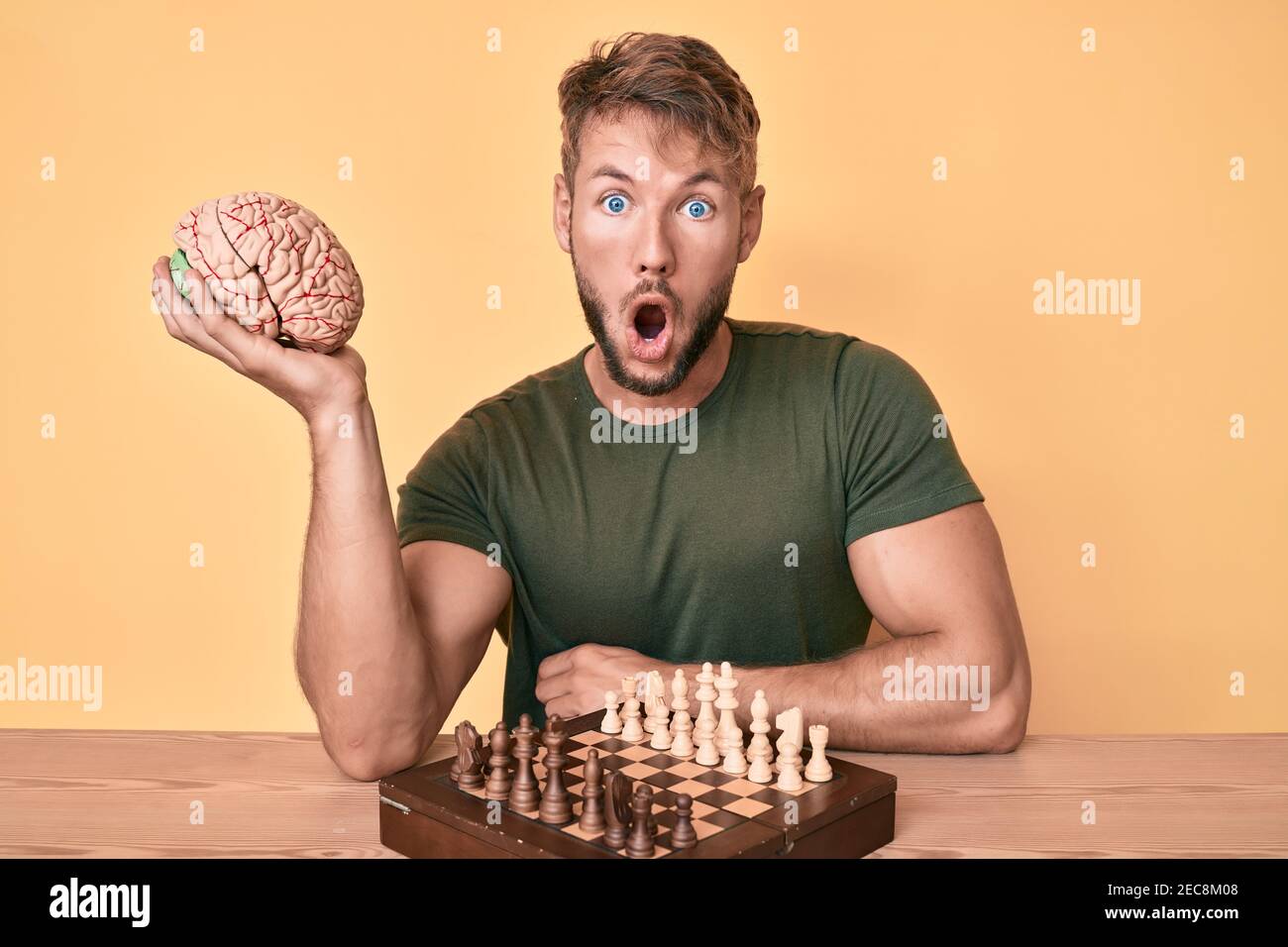 Young caucasian man holding brain while playing chess scared and amazed ...