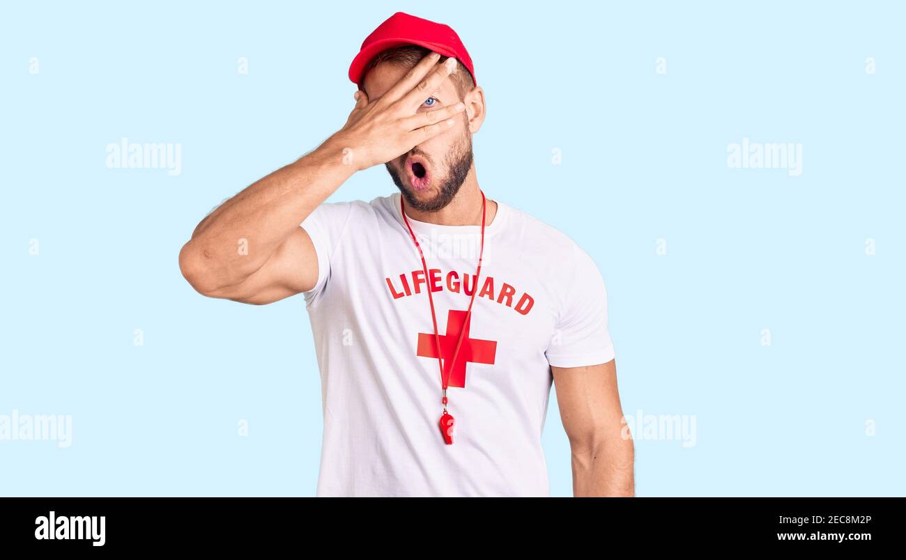 Young caucasian man wearing lifeguard t shirt holding whistle peeking ...