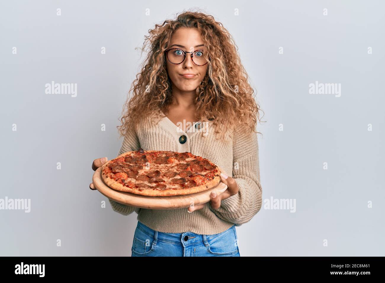 Beautiful caucasian teenager girl eating tasty pepperoni pizza skeptic ...