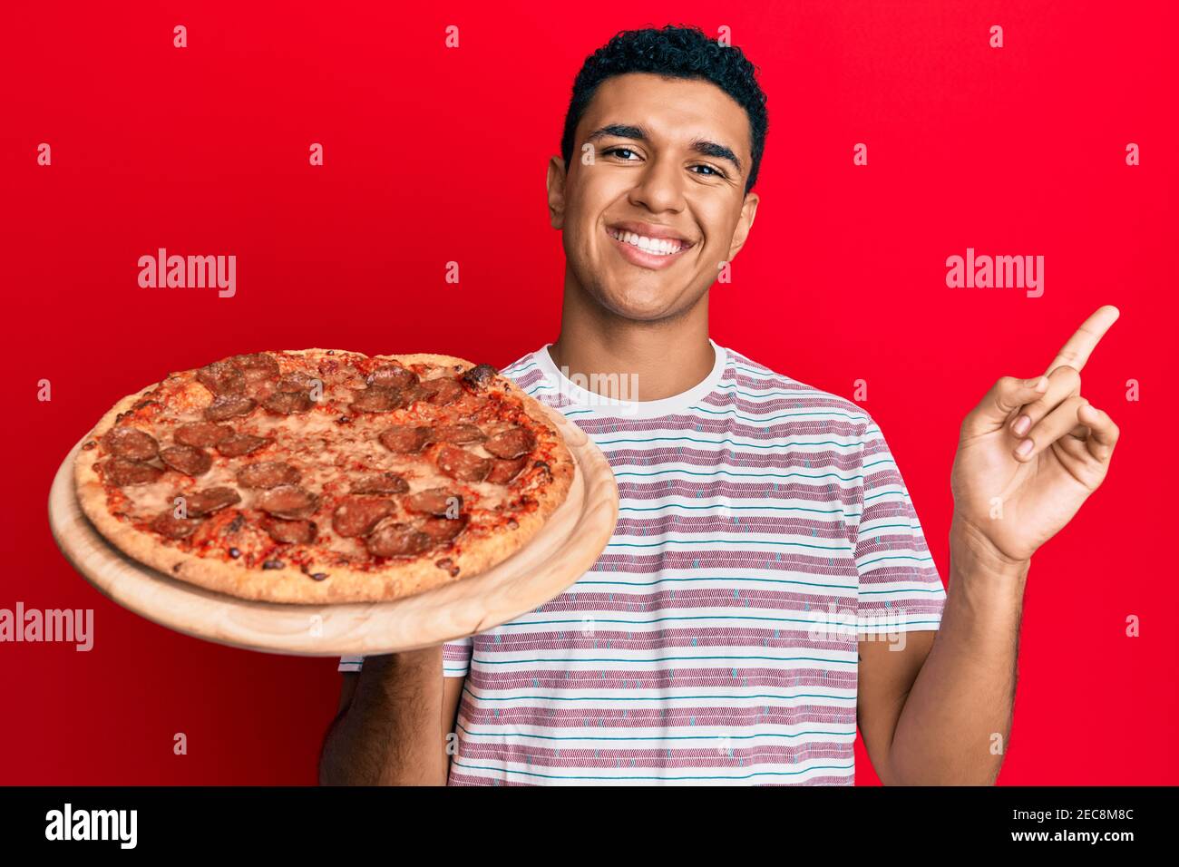 Young arab man holding italian pizza smiling happy pointing with hand ...