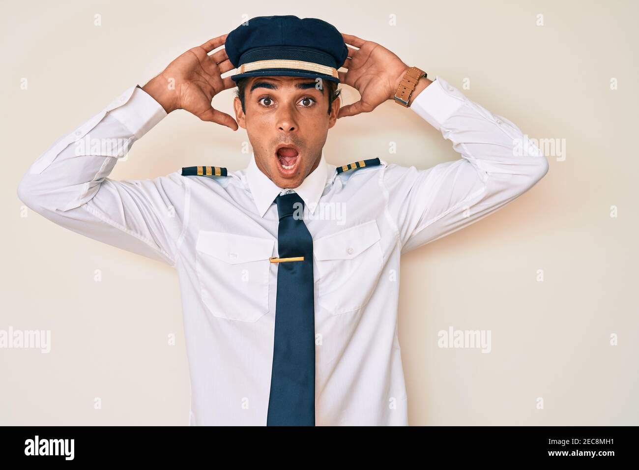Young hispanic man wearing airplane pilot uniform crazy and scared with ...