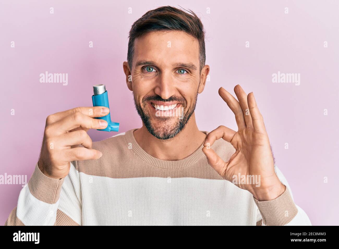 Handsome man with beard holding medical asthma inhaler doing ok sign ...