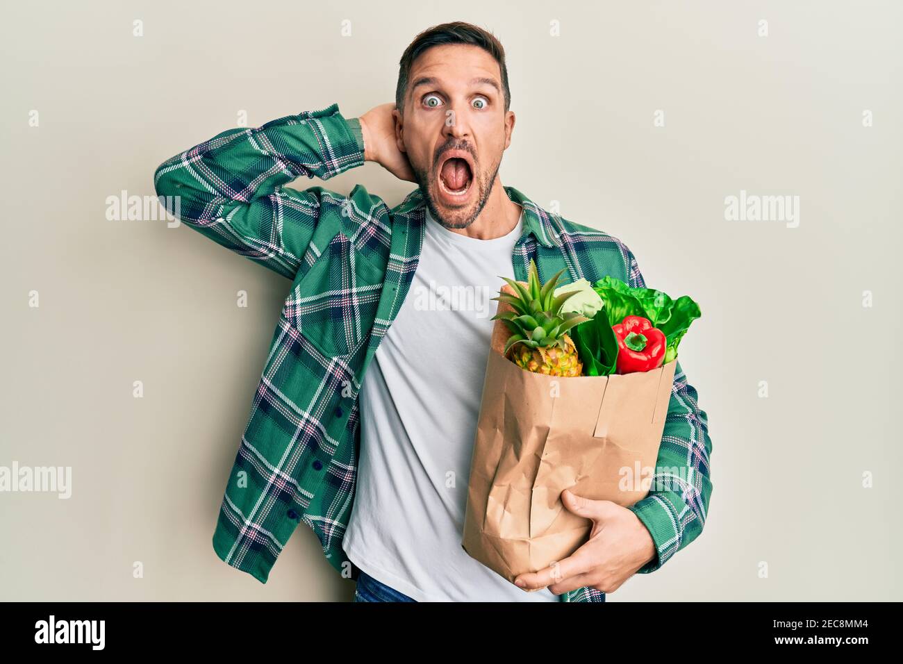 Handsome man with beard holding paper bag with groceries crazy and ...