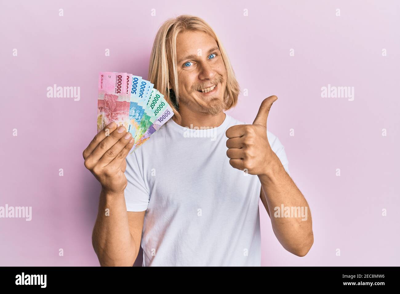Caucasian young man with long hair holding indonesian rupiah banknotes ...