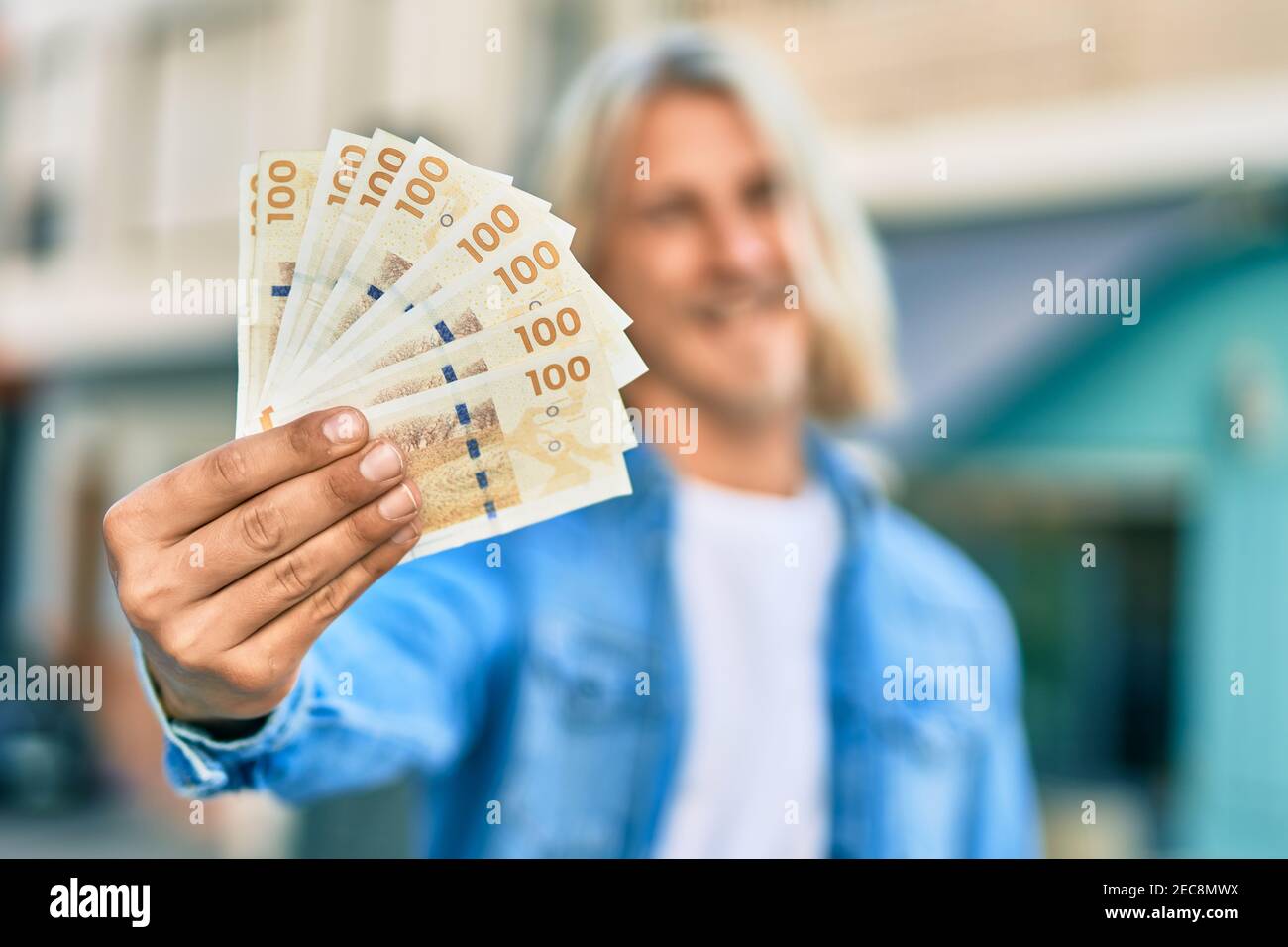 Young blond scandinavian man smiling happy holding danmark 100 kroner ...